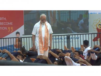 PM Modi helps participants correct their posture as they perform yoga ...